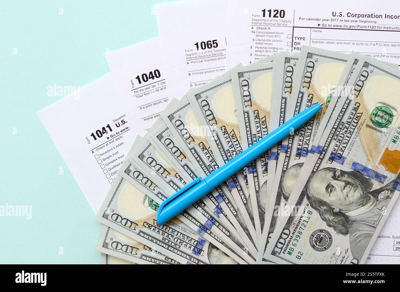 Tax forms lies near hundred dollar bills and blue pen on a light blue ...