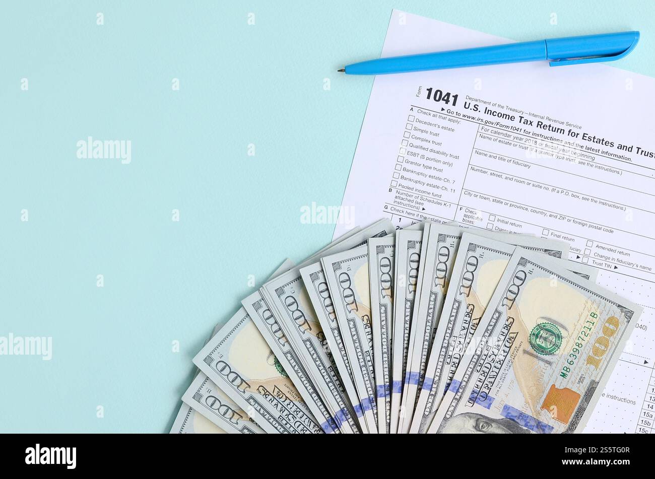 1041 tax form lies near hundred dollar bills and blue pen on a light ...