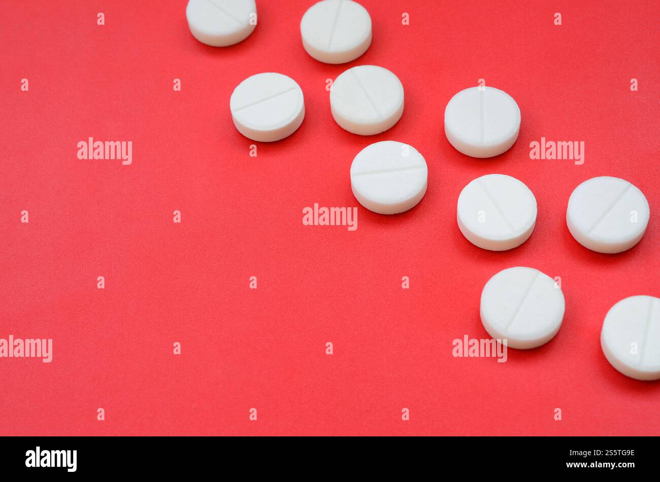 A few white tablets lie on a bright red background surface. Background ...