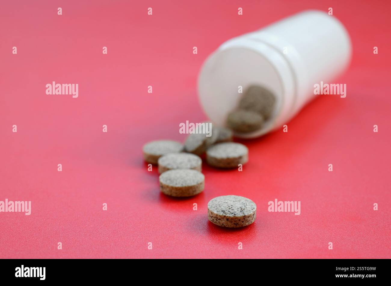 Several brown tablets fall out of the plastic jar on the red surface ...