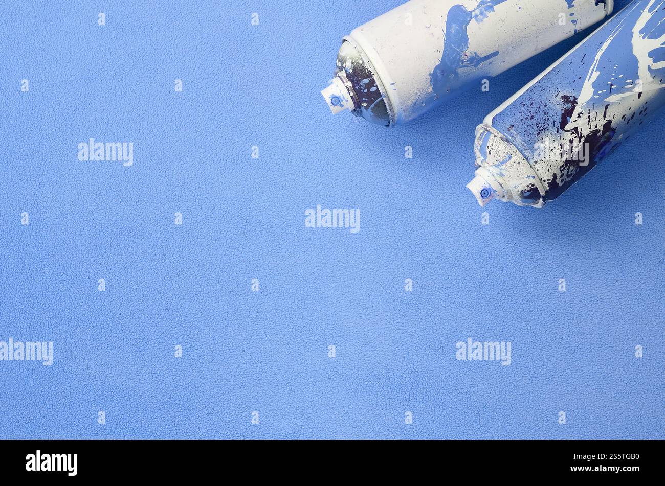 Some used blue aerosol spray cans with paint drips lies on a blanket of ...