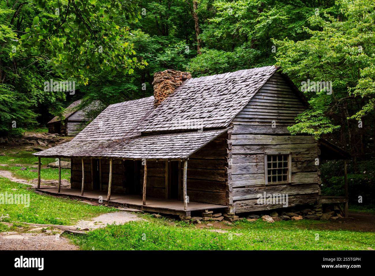 A small log cabin with a porch and a chimney. The cabin is surrounded ...