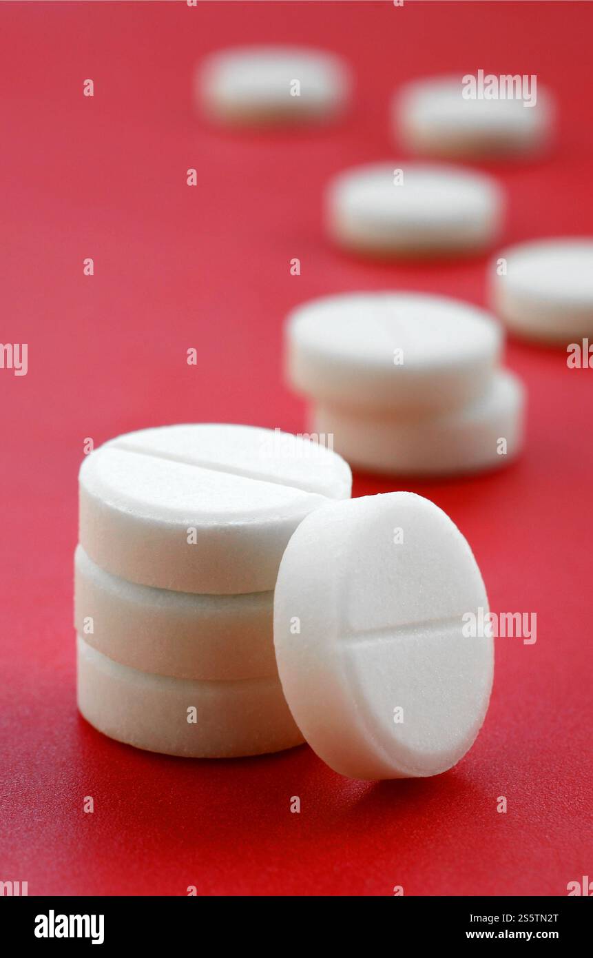 A few white tablets lie on a bright red background surface. Background ...