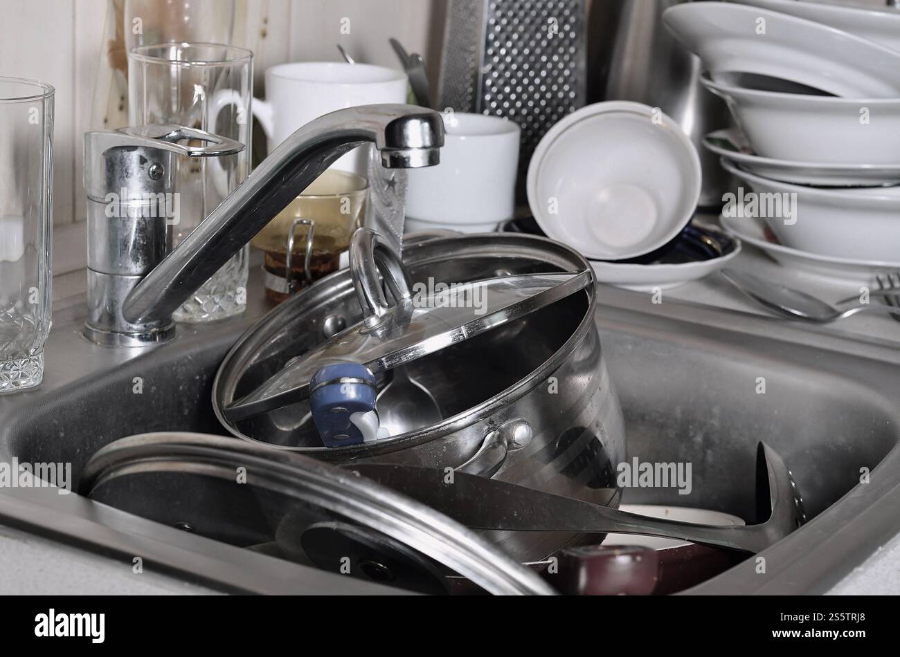 A huge pile of unwashed dishes in the kitchen sink and on the ...