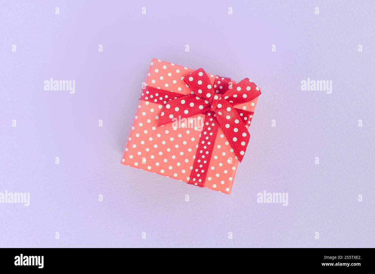 Small red gift box with ribbon lies on a violet background. Minimalism ...