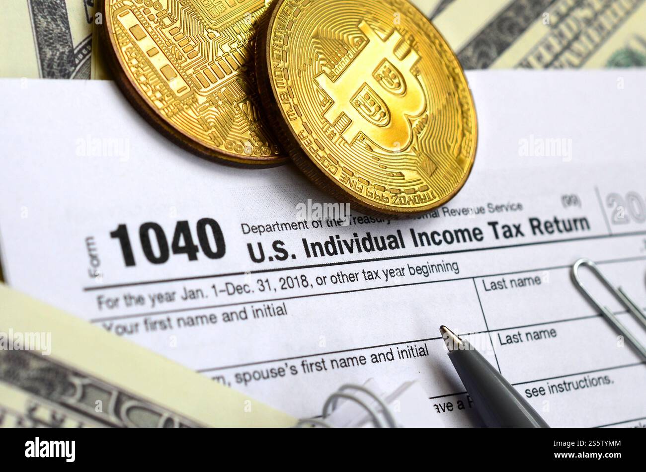 The pen, bitcoins and dollar bills is lies on the tax form 1040 U.S ...