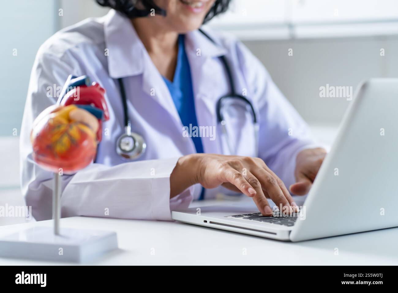 Doctor consult patient on laptop with anatomical model of human heart ...