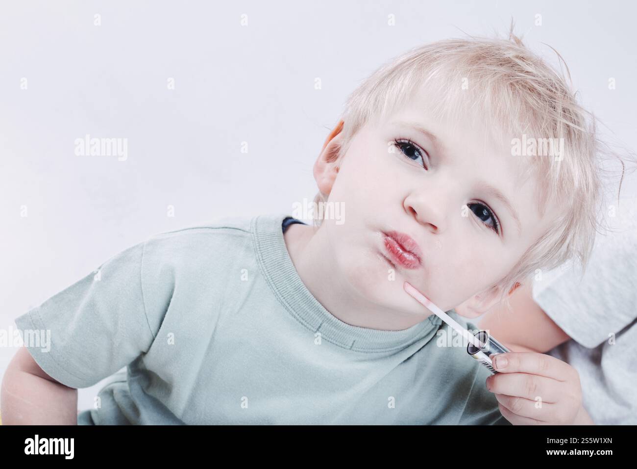 Toddler enjoying a playful moment while older sibling applying lip ...