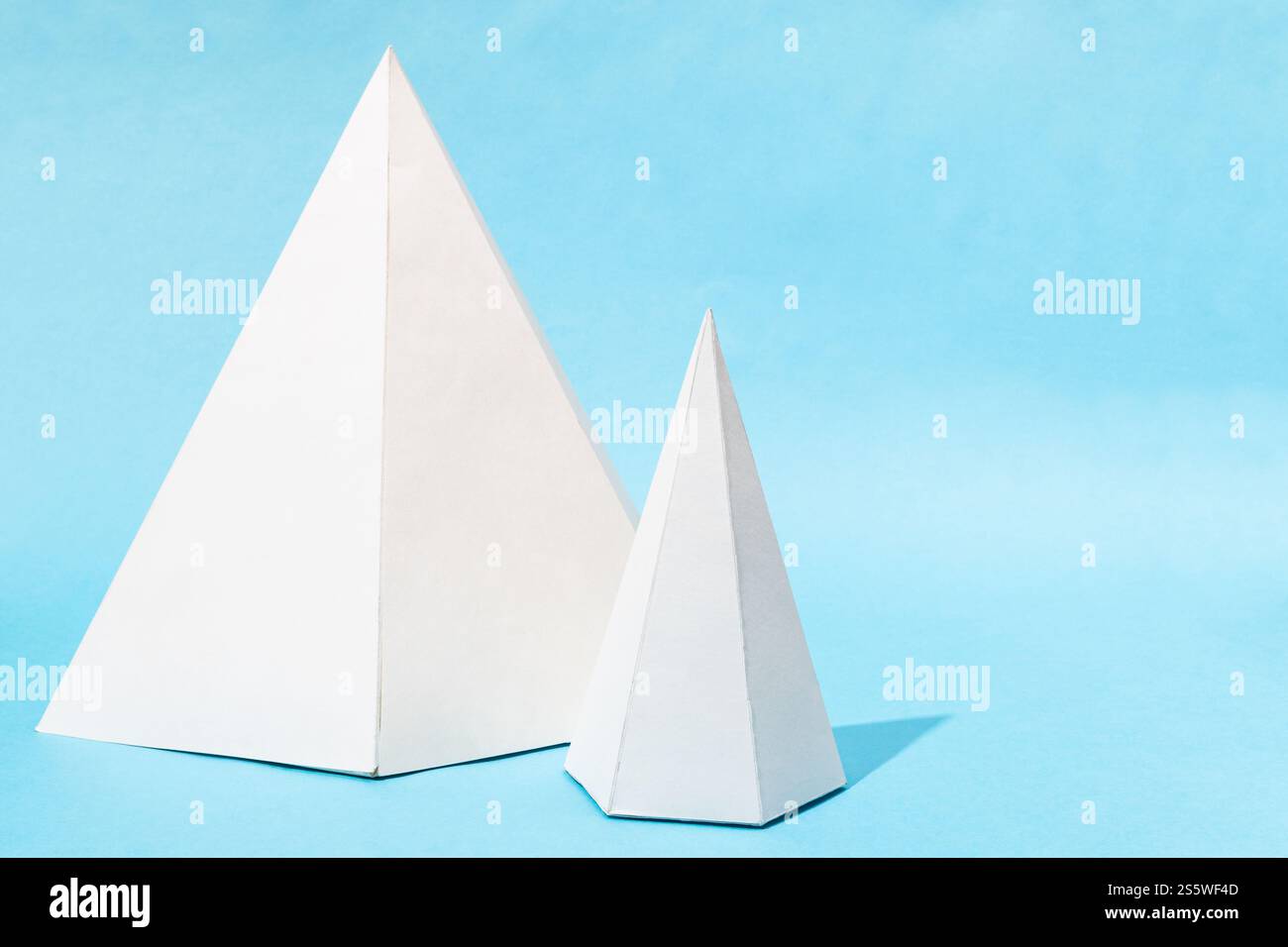 hand-crafted paper big and small lying pyramids on turquoise blue ...