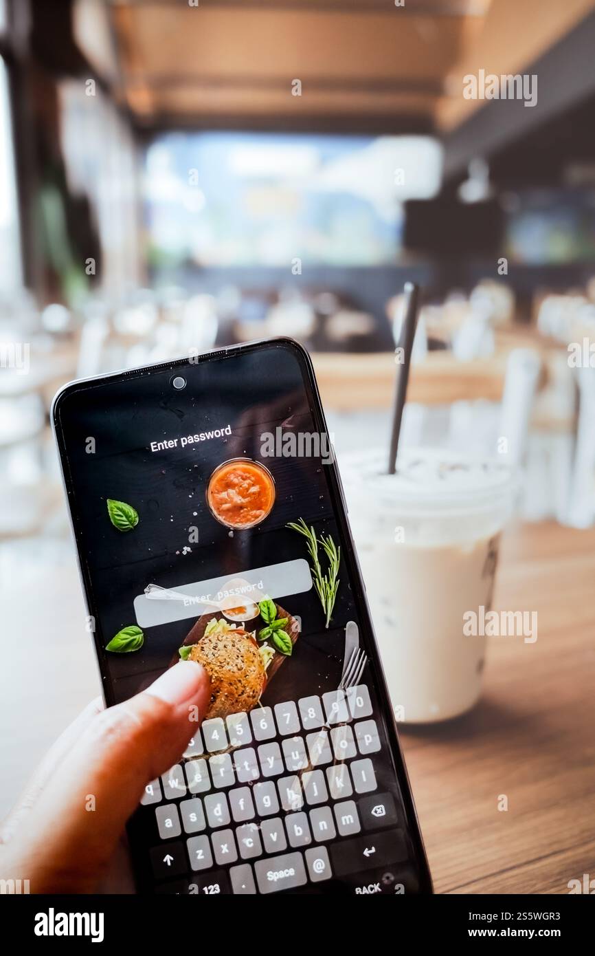 Hand entering password to unlock smartphone with iced coffee latte and ...