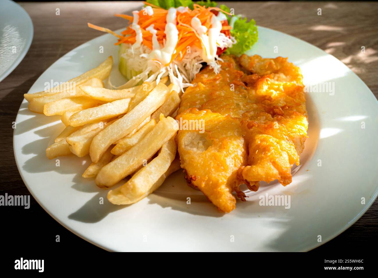 A plate of fried fries, flour fried fish and chopped vegetables served ...