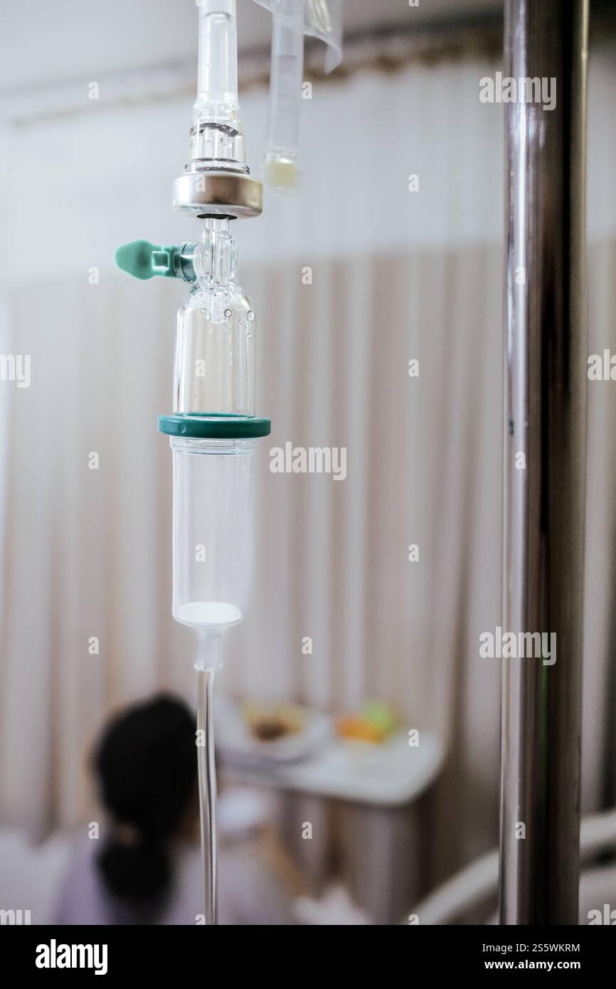 Closeup View of Intravenous Infusion Drip with Female Patient Sitting on Hospital Bed on the ...