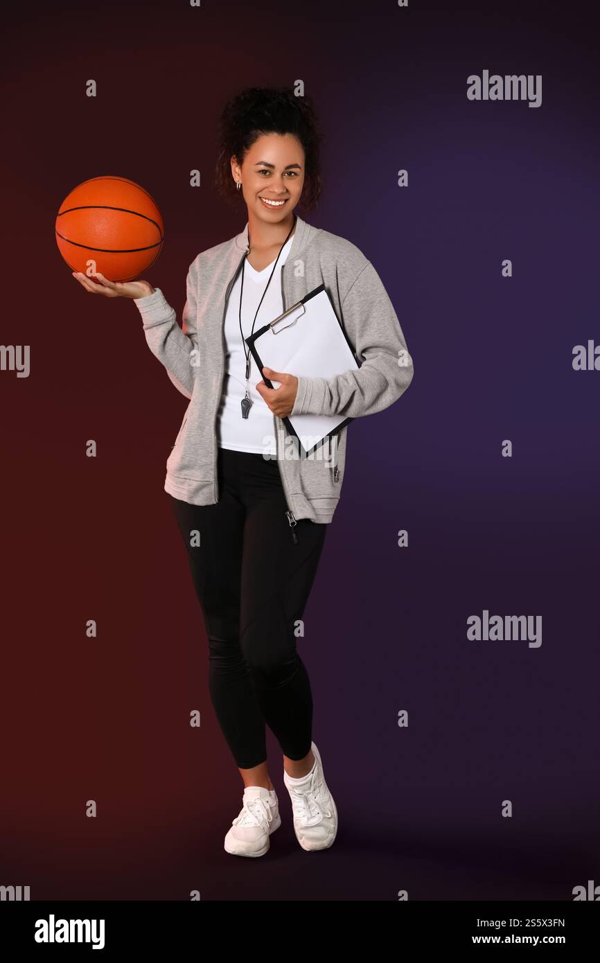 Female African-American basketball trainer with ball and clipboard on ...