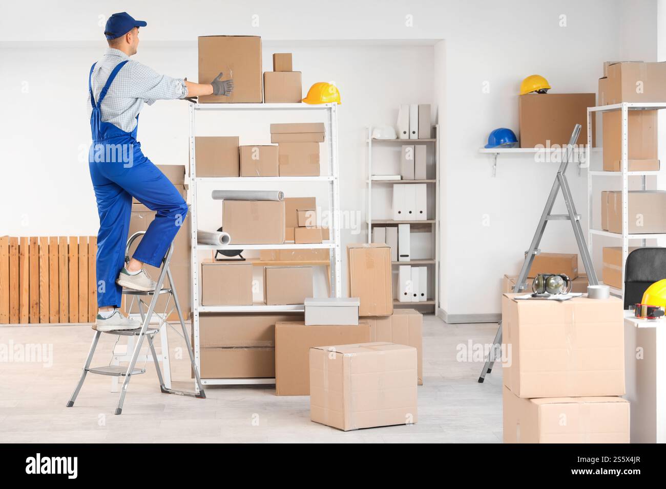 Male loader on stepladder taking box from shelf in warehouse, back view ...