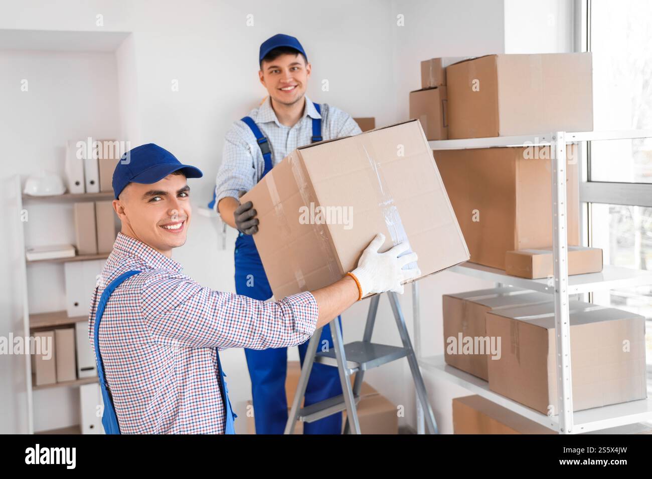 Male loaders with cardboard box in warehouse Stock Photo - Alamy