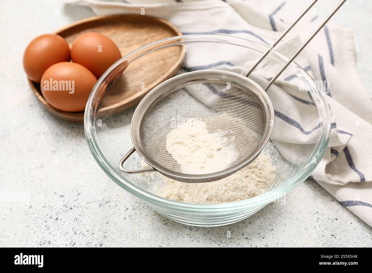 Metal sieve with flour in bowl, chicken eggs and napkin on light ...