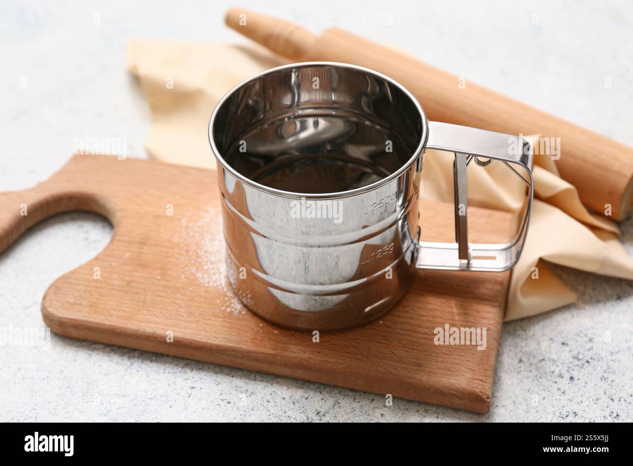 Metal flour sieve mug, wooden board, rolling pin and napkin on light ...