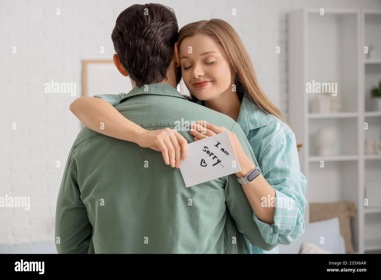 Young woman holding paper with text I AM SORRY and hugging her husband ...