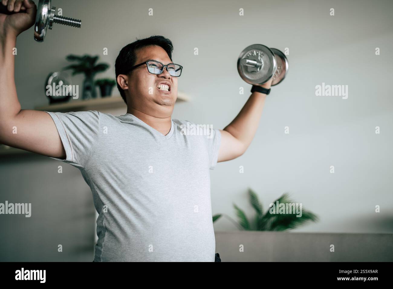 Funny overweight man wearing eyeglasses is standing and lifting up ...