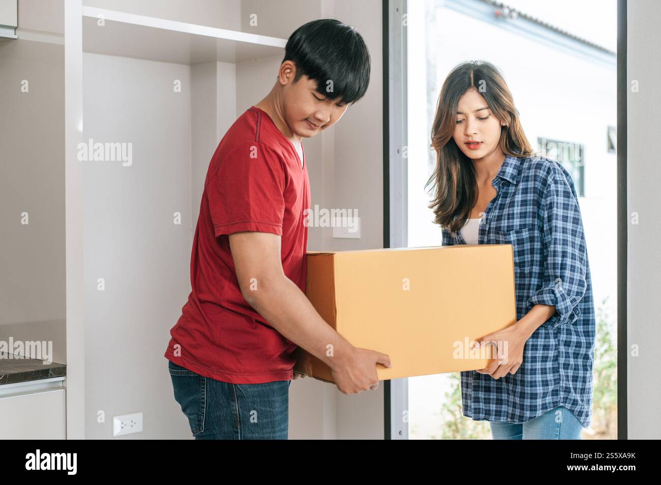 Young Asian couple help to holding heavy cardboard box walk into new ...