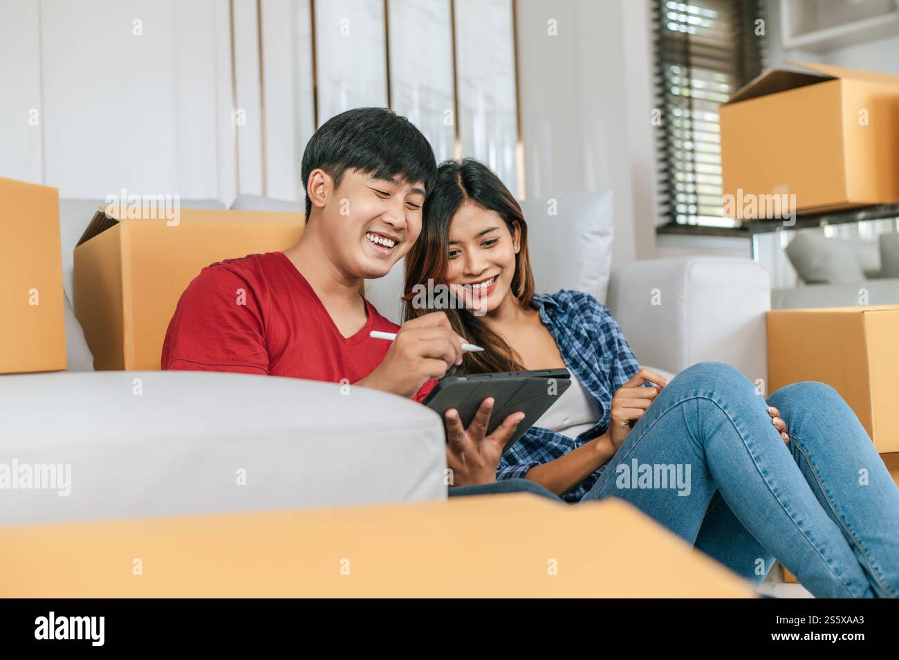 Young Asian couple sitting front of sofa on floor and use tablet while counting boxs after ...