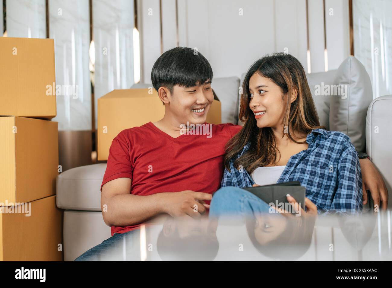 Young Asian couple sitting front of sofa on floor and use tablet while counting boxs after ...