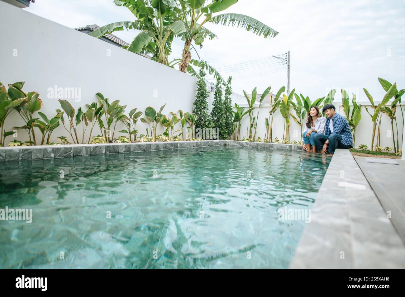 Young Asian couple enjoy together while rest near swimming pool at new ...