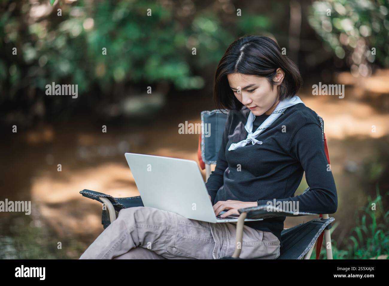 Young woman sitting on camping chair and use laptop computer while ...