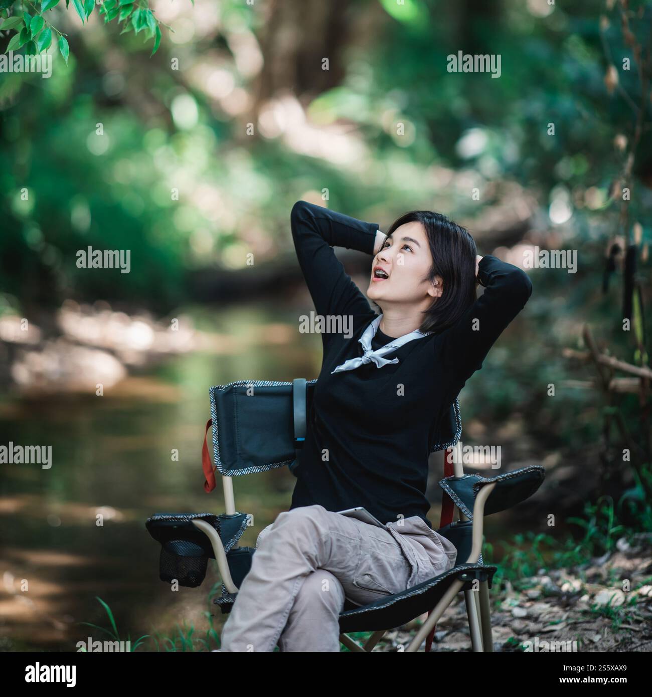 Happily young woman sitting on chair while relax time on camping in ...