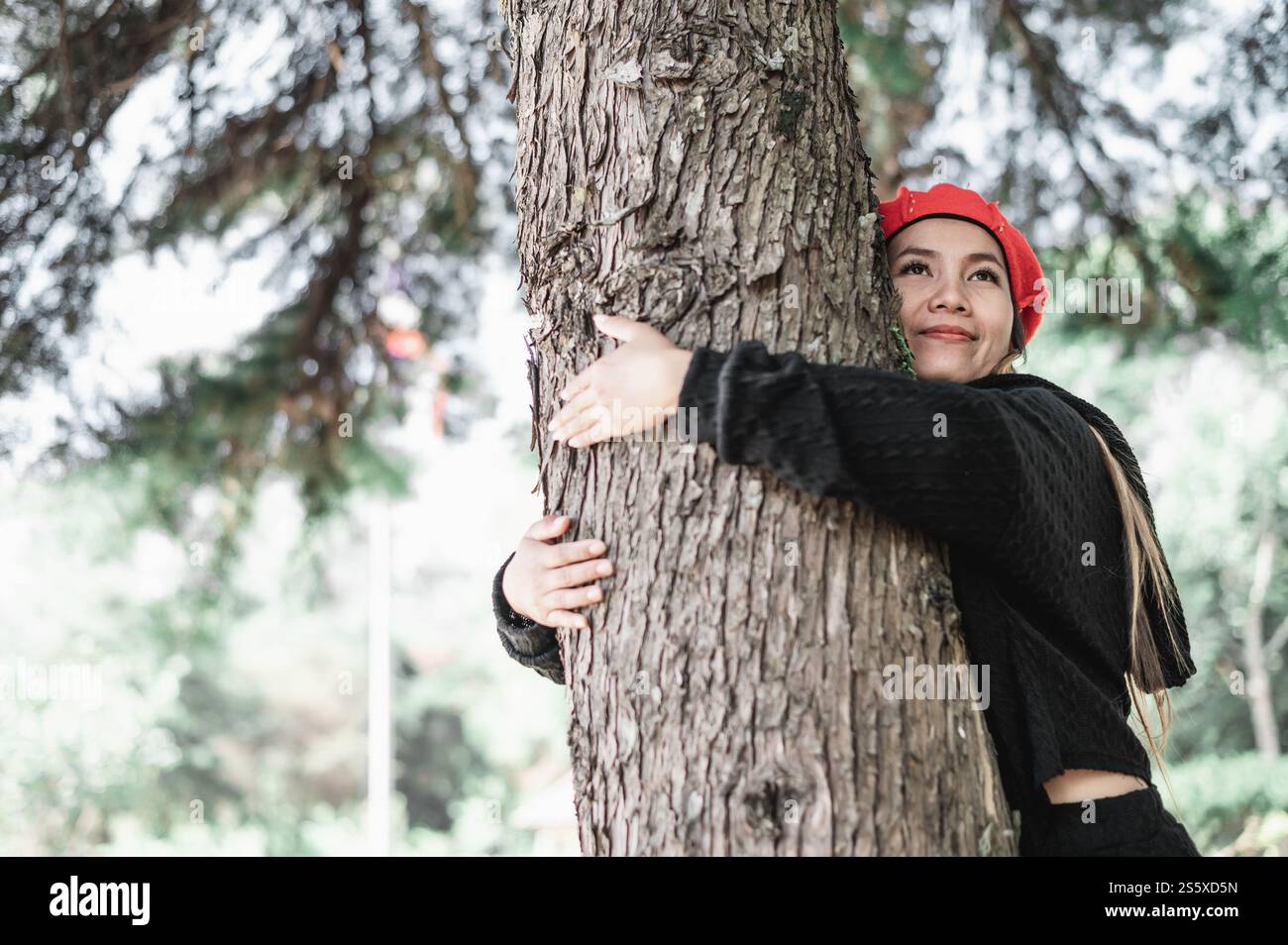 Contented young woman hugging a large tree with a blissful expression ...