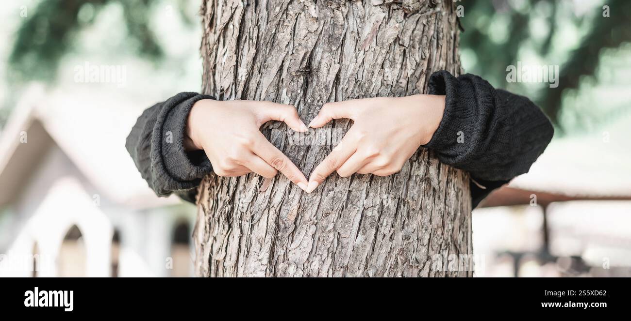Young woman hug a tree in the forest and show a sign of heart and love ...