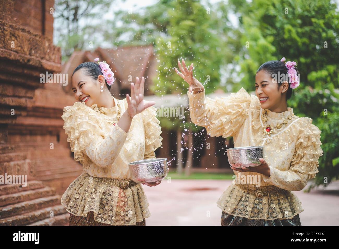 Young smiling women dress in beautiful Thai costumes splashing water in temples and preserve the ...