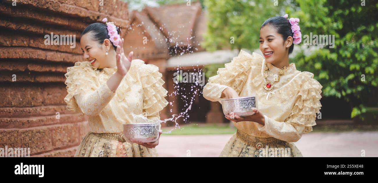 Young smiling women dress in beautiful Thai costumes splashing water in temples and preserve the ...