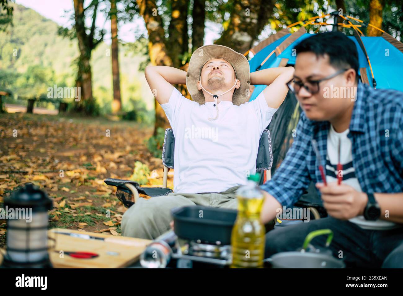 Asian relaxed man sitting and waiting for his friend cooking with tent ...