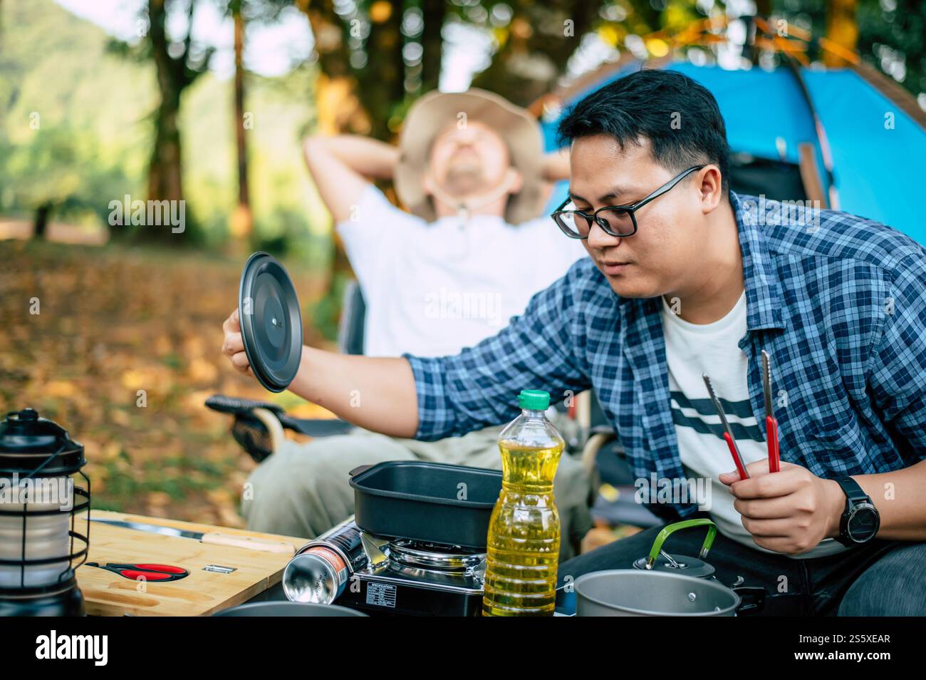 Asian relaxed man sitting and waiting for his friend cooking with tent ...
