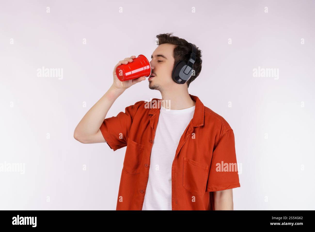 Portrait of a handsome young man with headphone standing and drinking coffee isolated white ...