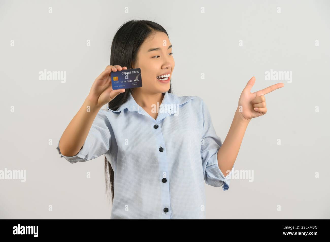 Portrait of positive young asian woman showing credit card good mood salary and pointing finger ...