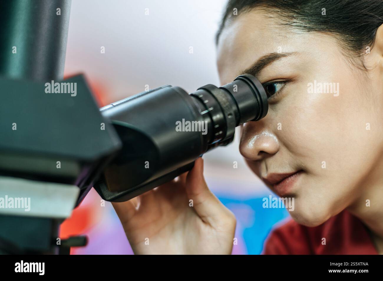Asian young female farmer looking through a microscope in a laboratory ...