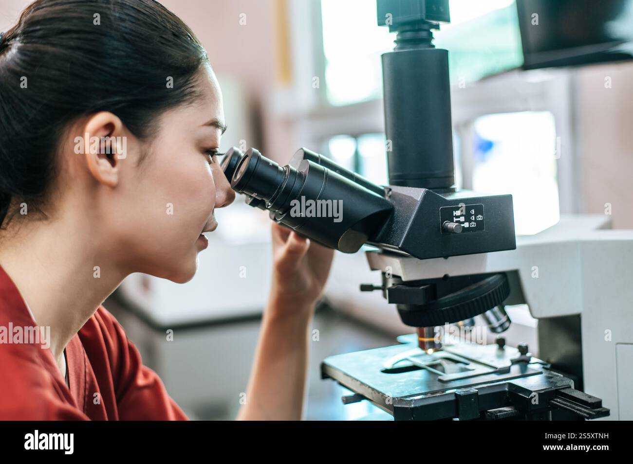 Asian young female farmer looking through a microscope in a laboratory. Modern technologies in ...