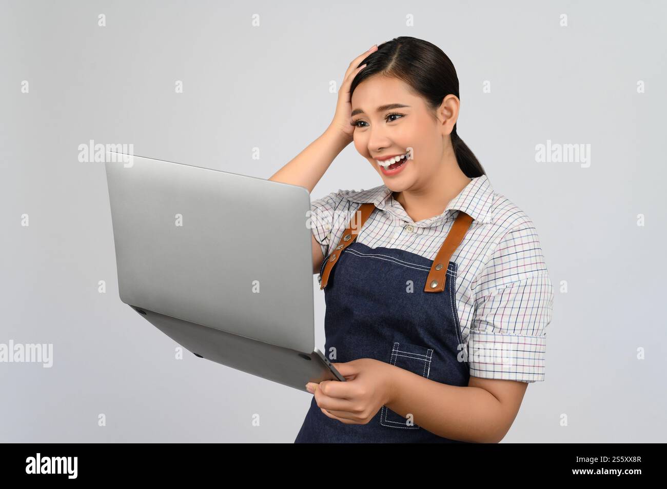 Portrait of young asian woman in waitress uniform looking on laptop ...