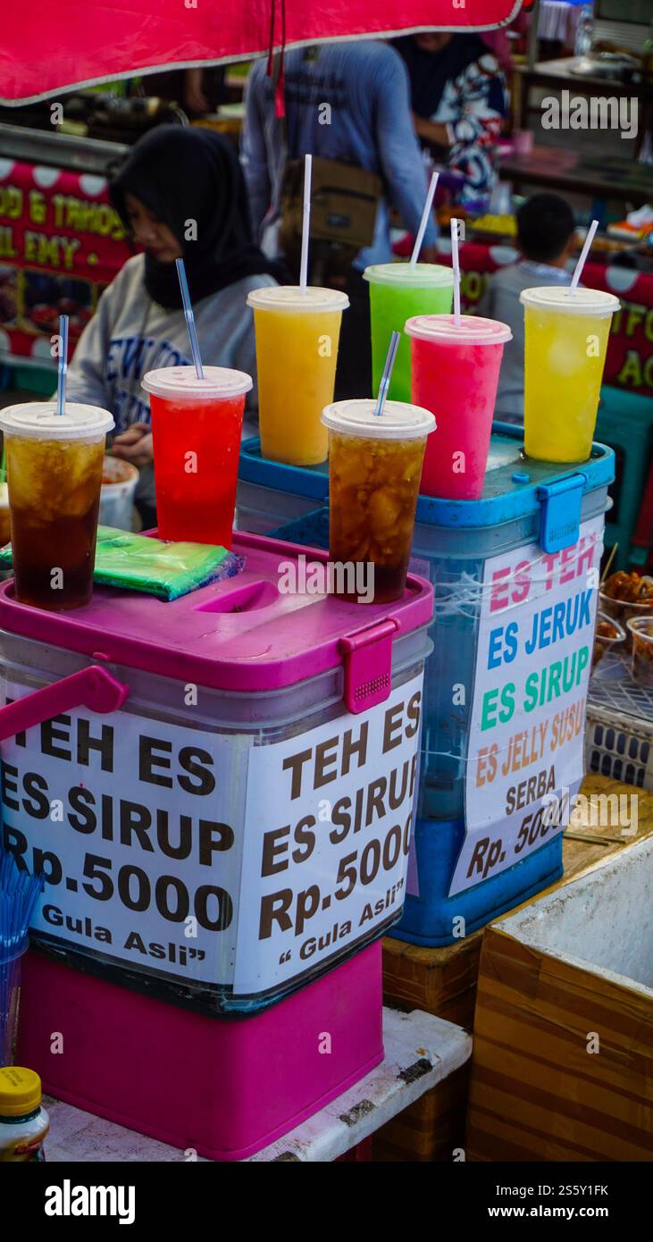 Colorful iced drinks in plastic cups displayed at a street market stall ...