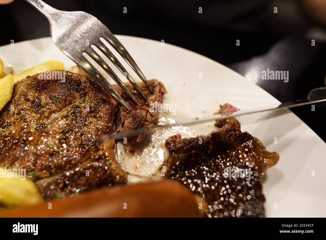 Man eating Grilled Meats stake from plate. hand holding knife and fork ...