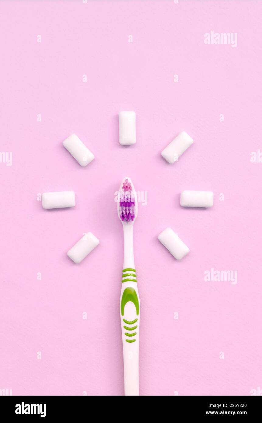 Toothbrush and chewing gums lie on a pastel pink background. Top view ...