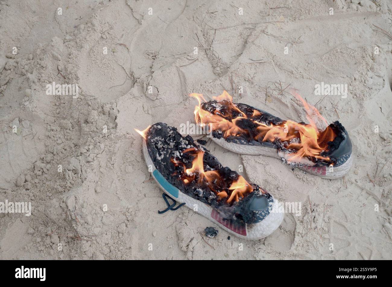 Burning sports sneakers or gym shoes on fire stand on sandy beach coast ...