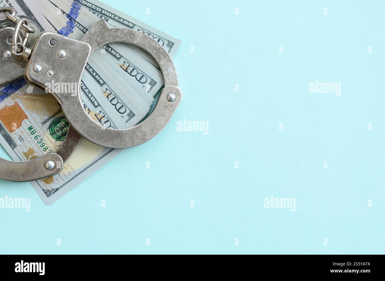 Silver police handcuffs and hundred dollar bills lies on light blue ...