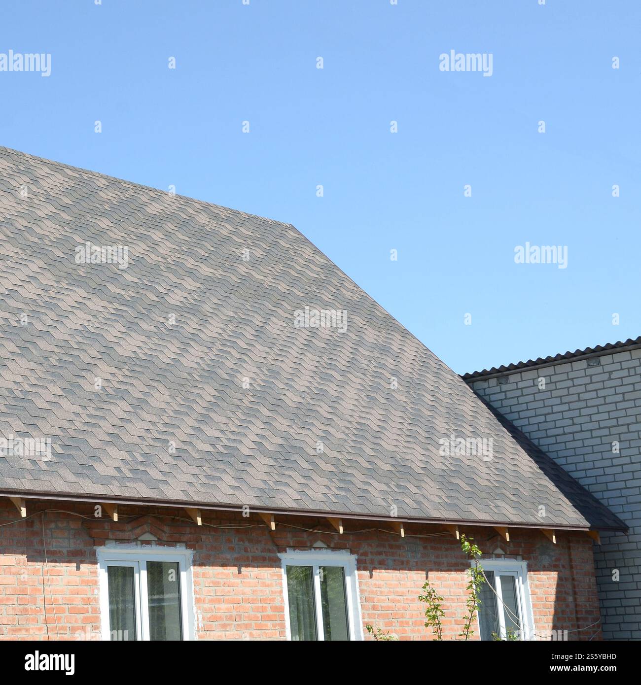 Flexible shingles of bitumen roofing surface on the brick house. Mosaic ...