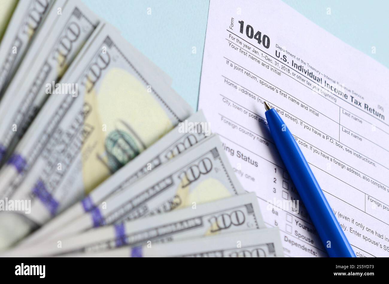 1040 tax form lies near hundred dollar bills and blue pen on a light ...