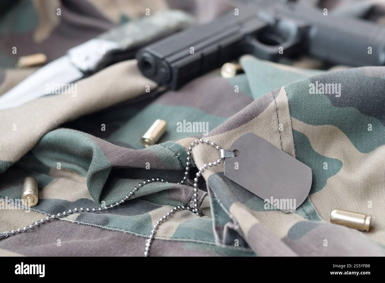 Army Dog tag token with 9mm bullets and pistol lie on folded camouflage ...