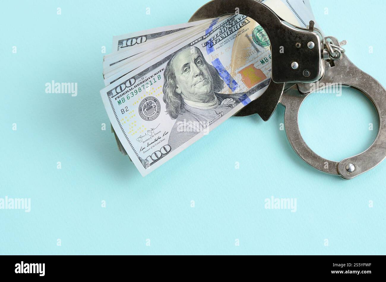 Silver police handcuffs and hundred dollar bills lies on light blue ...