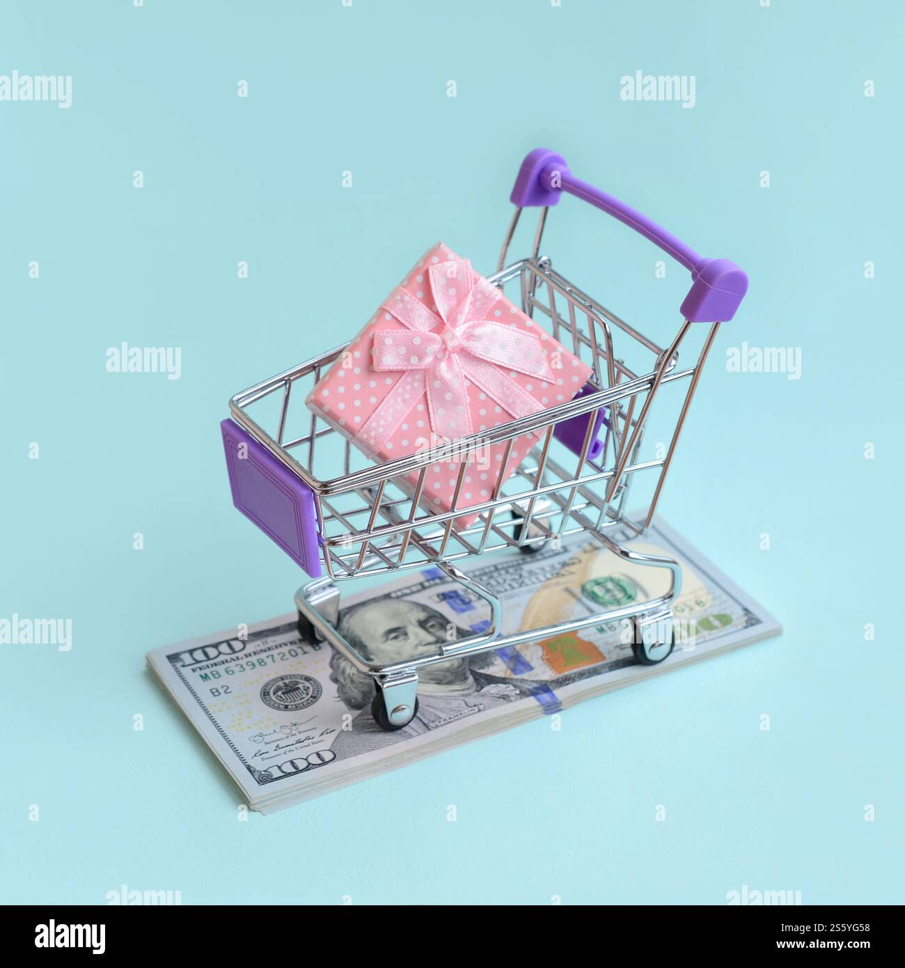 Gift box in a small shopping cart lies on a dollar bills on light blue ...